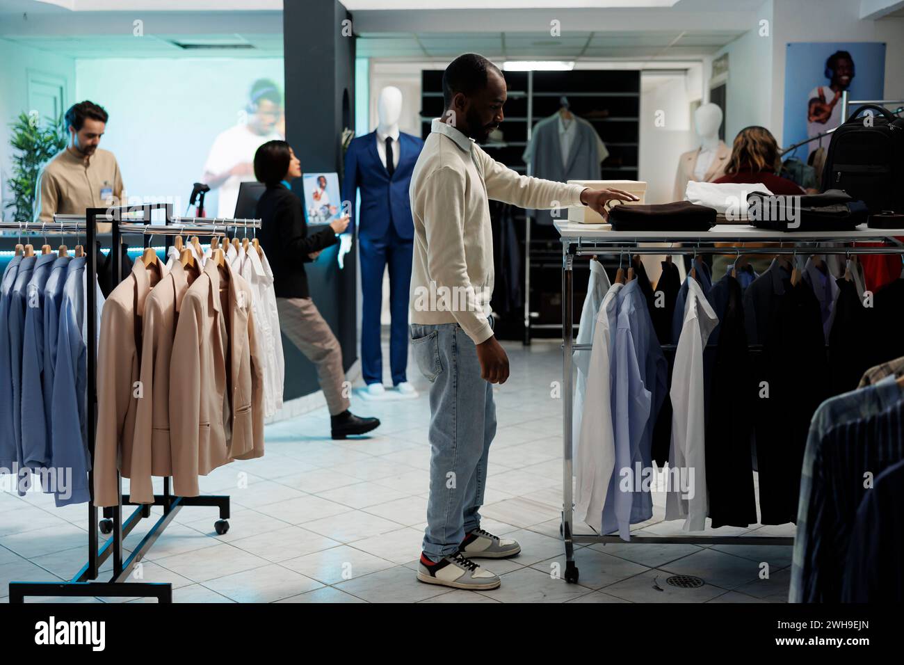 Stylish man searching for clothes and taking apparel from shelf in ...