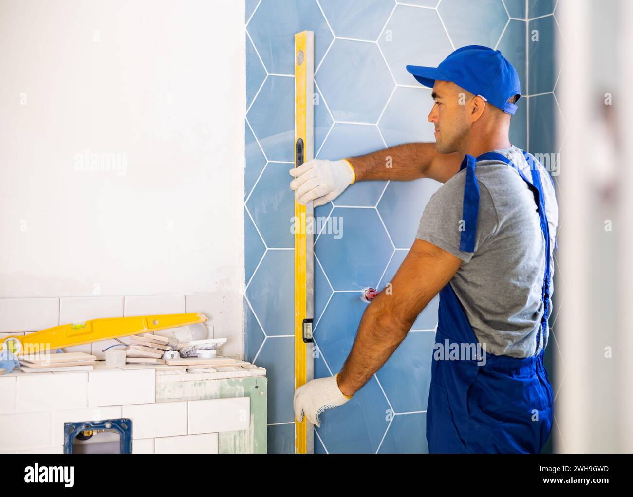 Master wearing work clothes checking vertical of installing tiles using ...