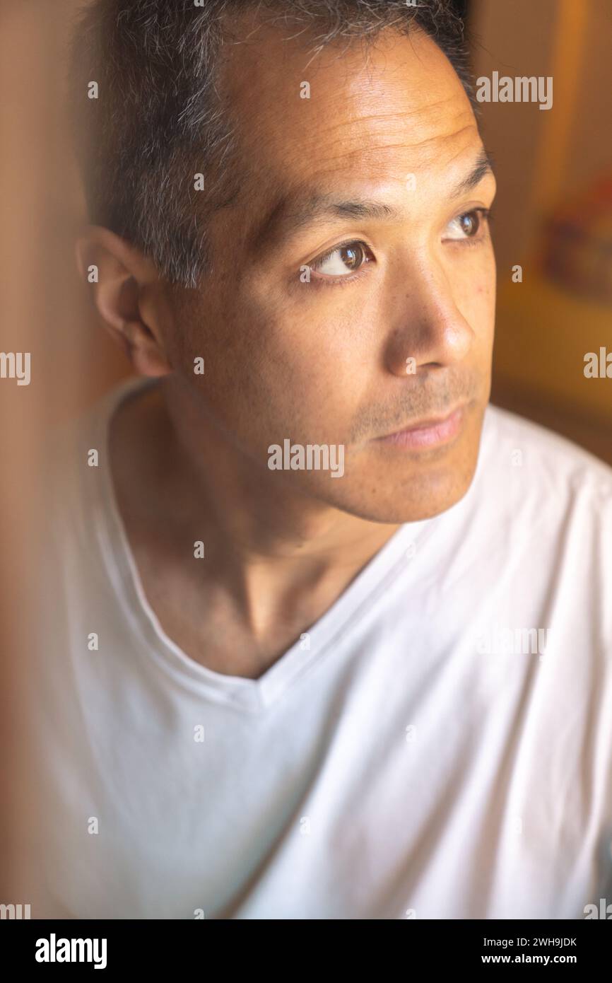 Vertical portrait of young Japanese man gazing out of a window with a ...