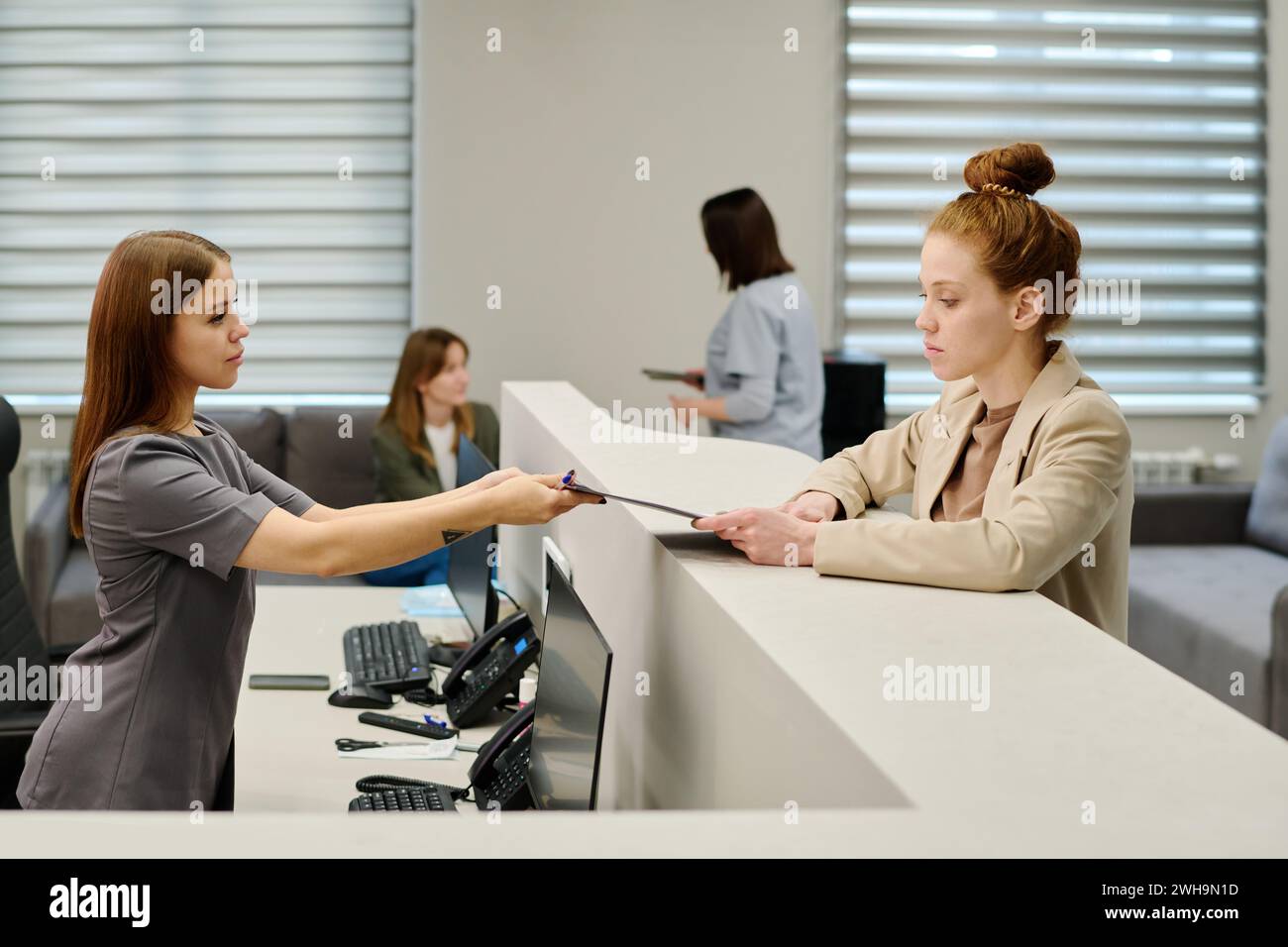 Young female receptionist in grey uniform helping female client with ...