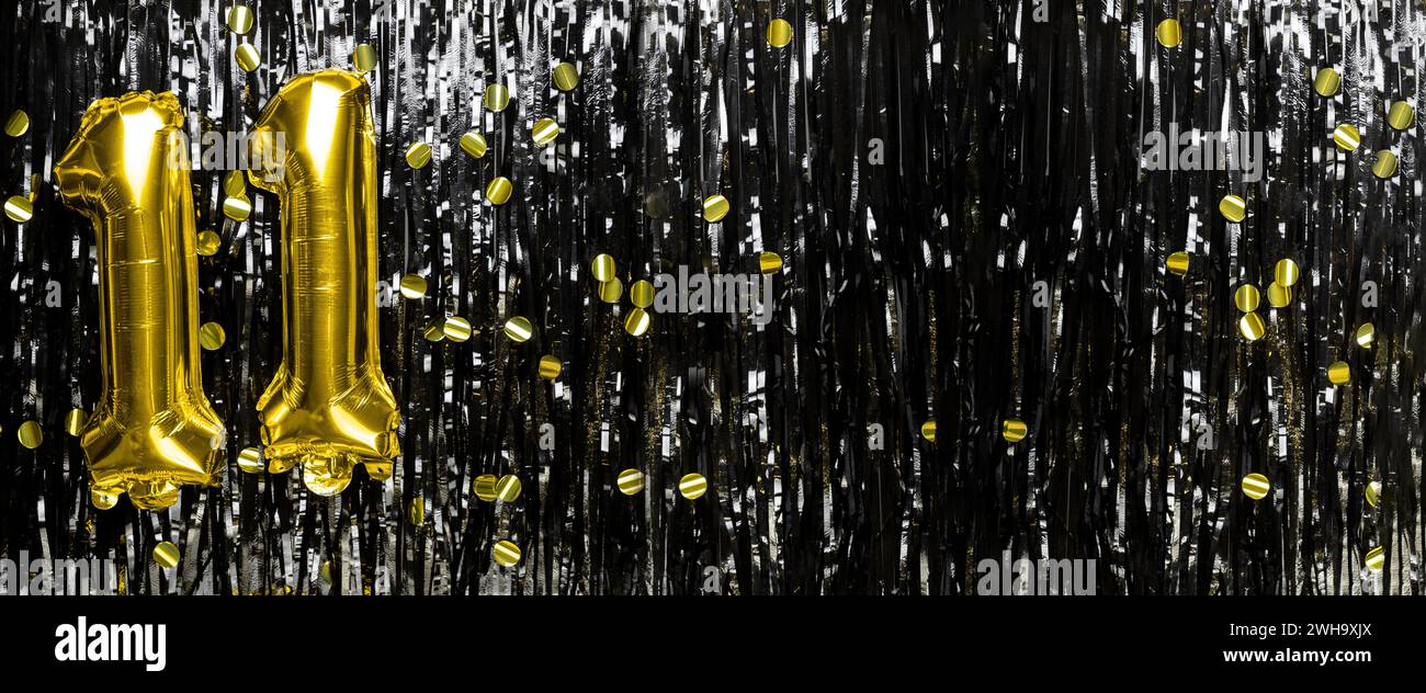 Gold foil balloon number number 11 on a background of black tinsel ...