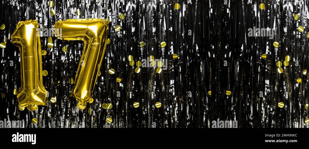 Gold foil balloon number number 17 on a background of black tinsel ...