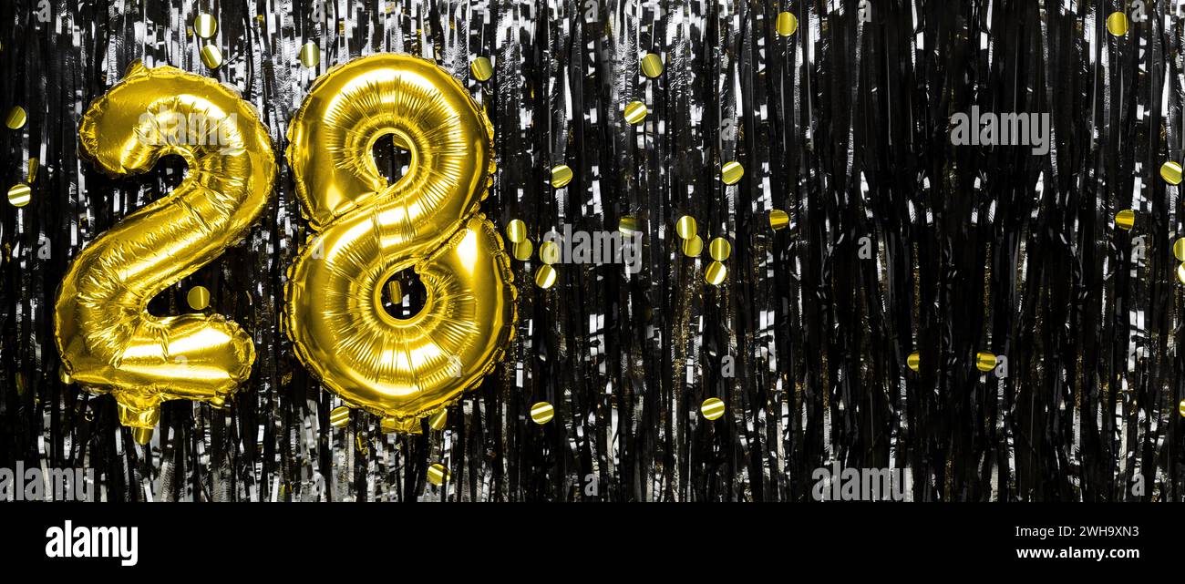 Gold foil balloon number number 28 on a background of black tinsel ...