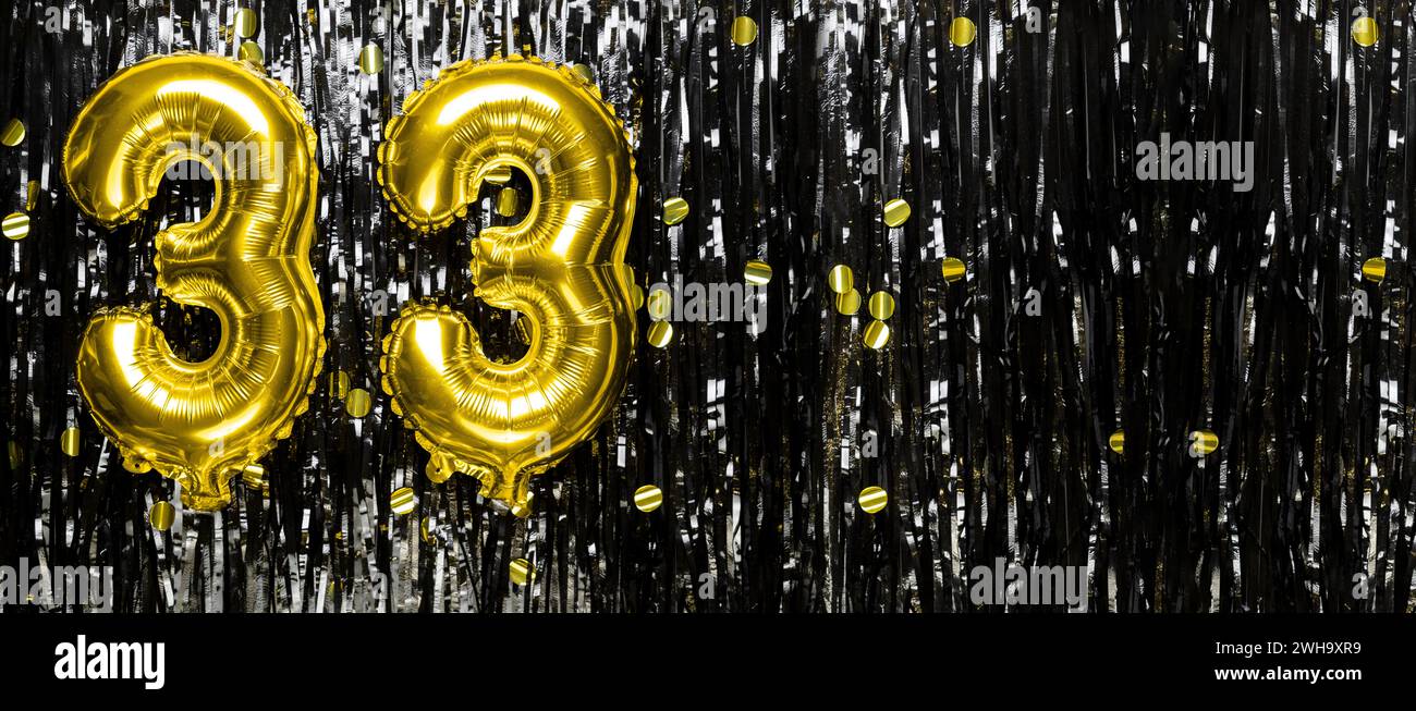Gold foil balloon number number 33 on a background of black tinsel ...
