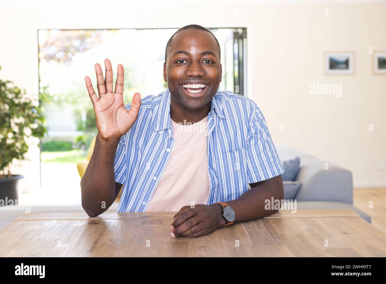 Young African American man waves cheerfully at home on a video call ...
