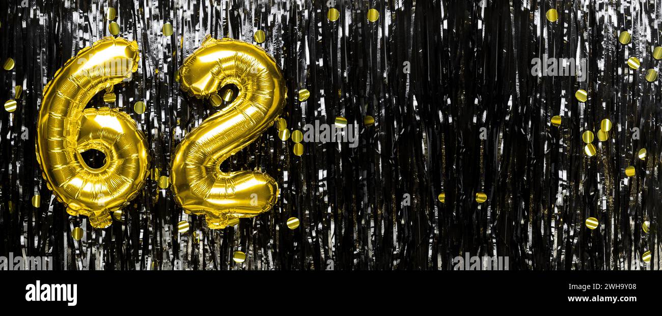 Gold foil balloon number number 62 on a background of black tinsel ...