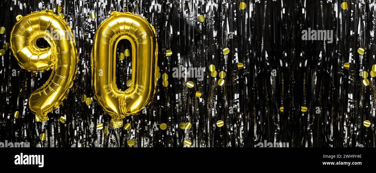 Gold foil balloon number number 90 on a background of black tinsel decoration. Birthday greeting ...