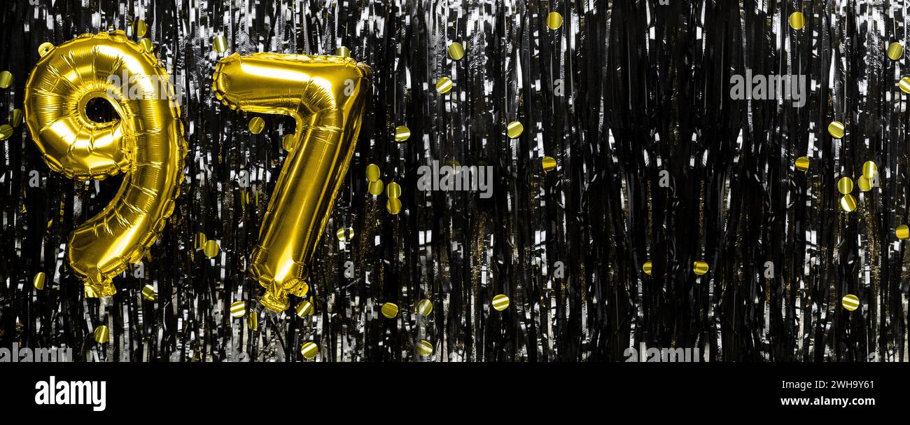 Gold foil balloon number number 97 on a background of black tinsel decoration. Birthday greeting ...