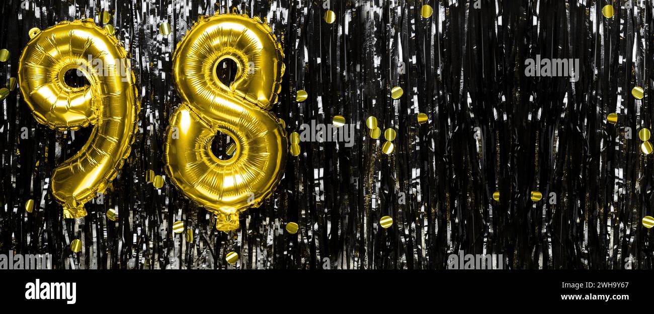 Gold foil balloon number number 98 on a background of black tinsel decoration. Birthday greeting ...