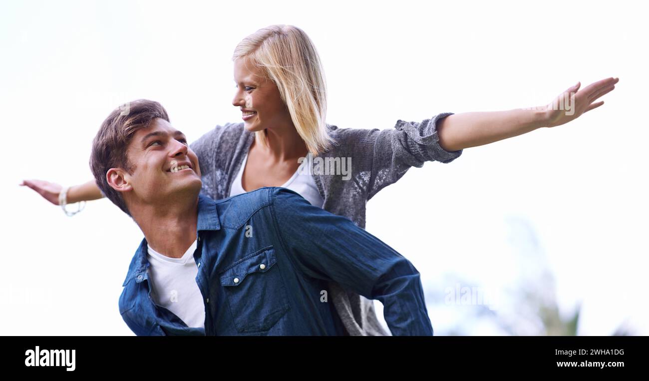 Couple, piggy back and plane with arms, smile or game by trees with ...