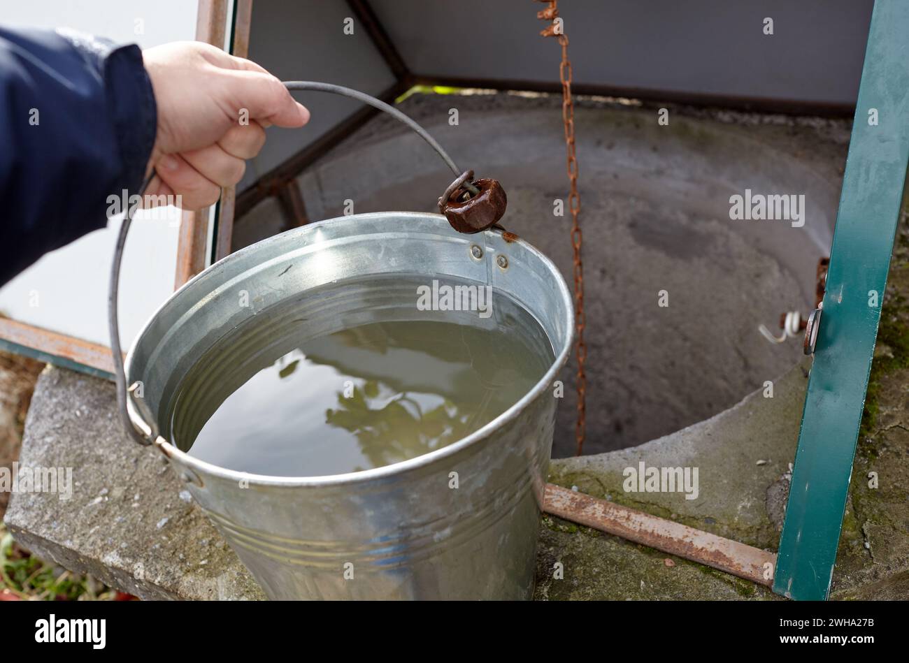 Man hand holding metal bucket with fresh water. Water from a deep well ...