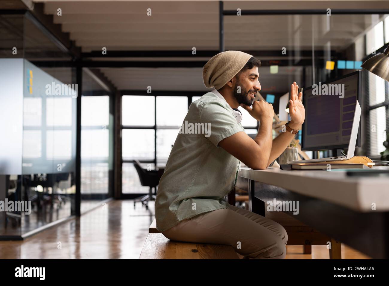 Young Asian man waves during a casual business video call in an office ...