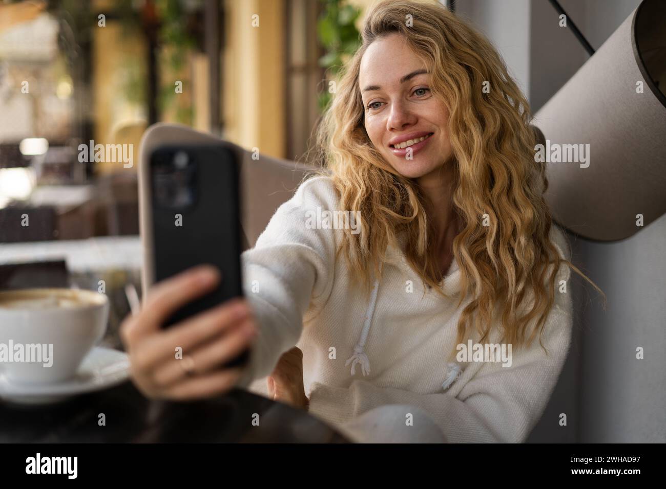 Beautiful millennial woman taking selfie and drinking aromatic coffee ...