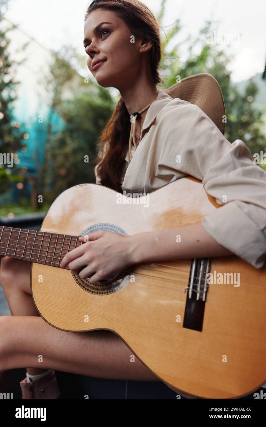 A woman sitting on a bench playing an acoustic guitar with her feet on ...