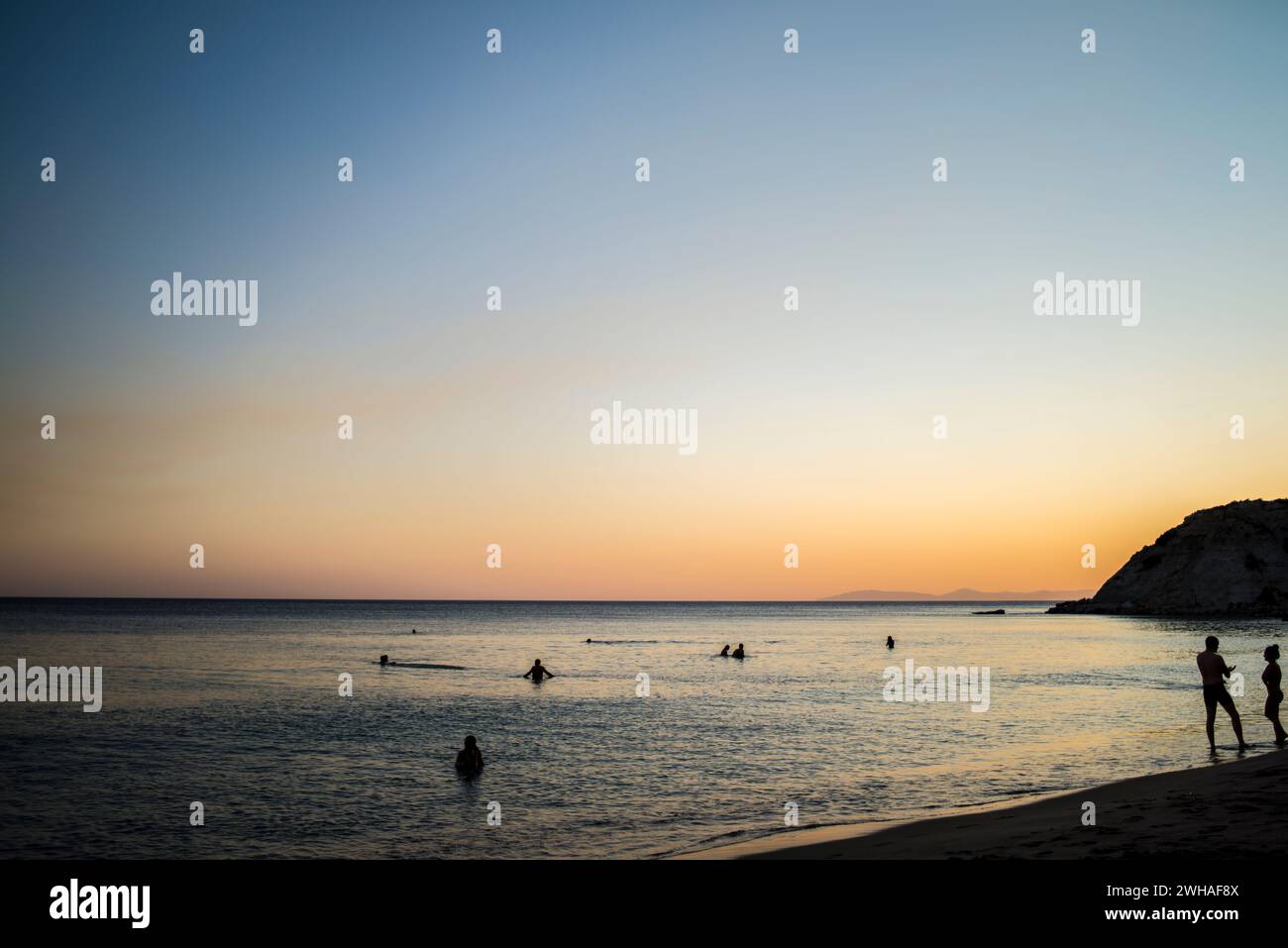 A tranquil scene as people enjoy a sunset swim in the calm sea, bathed ...