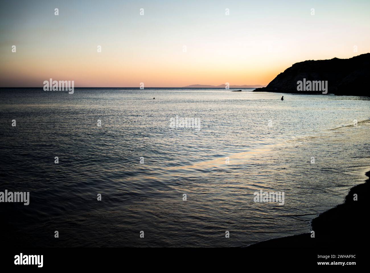 A tranquil scene as people enjoy a sunset swim in the calm sea, bathed ...