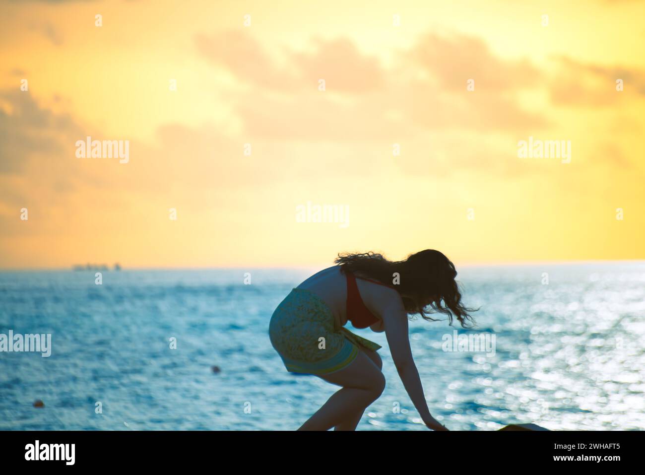 A woman on a Maldives dock, picking something from the sandy ground ...