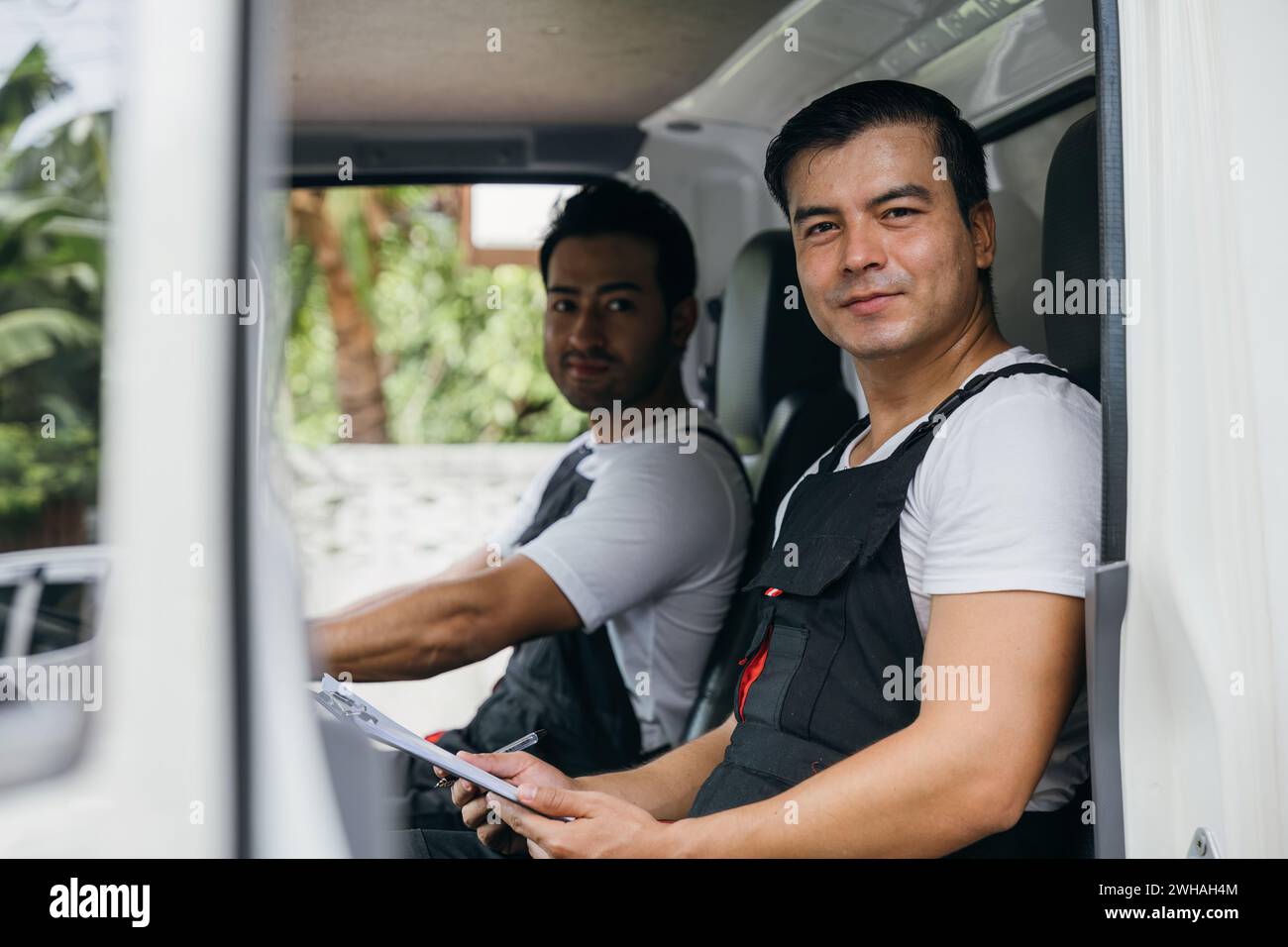 Mover workers an ethnically diverse team driving a truck for relocation service. Confidently ...