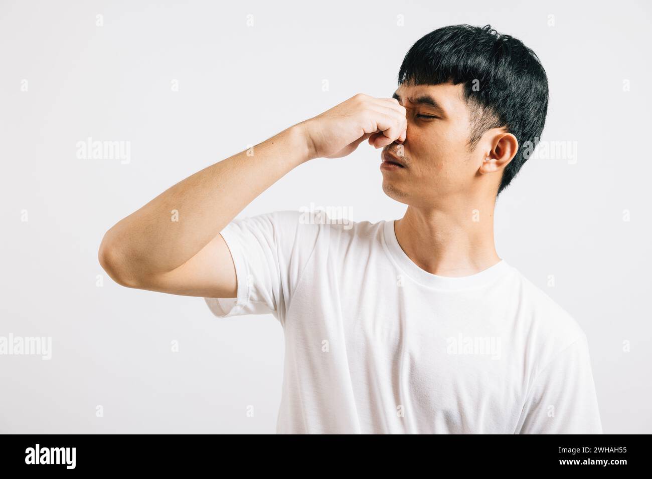 Asian man wearing an anxious expression while pinching his nose due to ...