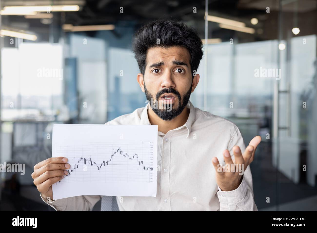 A man with a beard is holding a paper with a graph, making a gesture ...