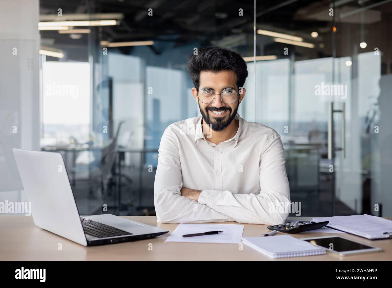 A white-collar worker sits at a desk with crossed arms, working on a ...