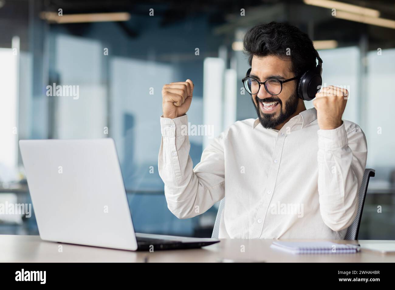 Indian businessman in a shirt at his desk with a laptop, celebrating a ...