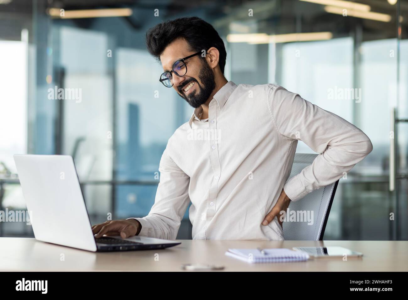 Indian man in glasses feeling back pain while working overtime at his ...