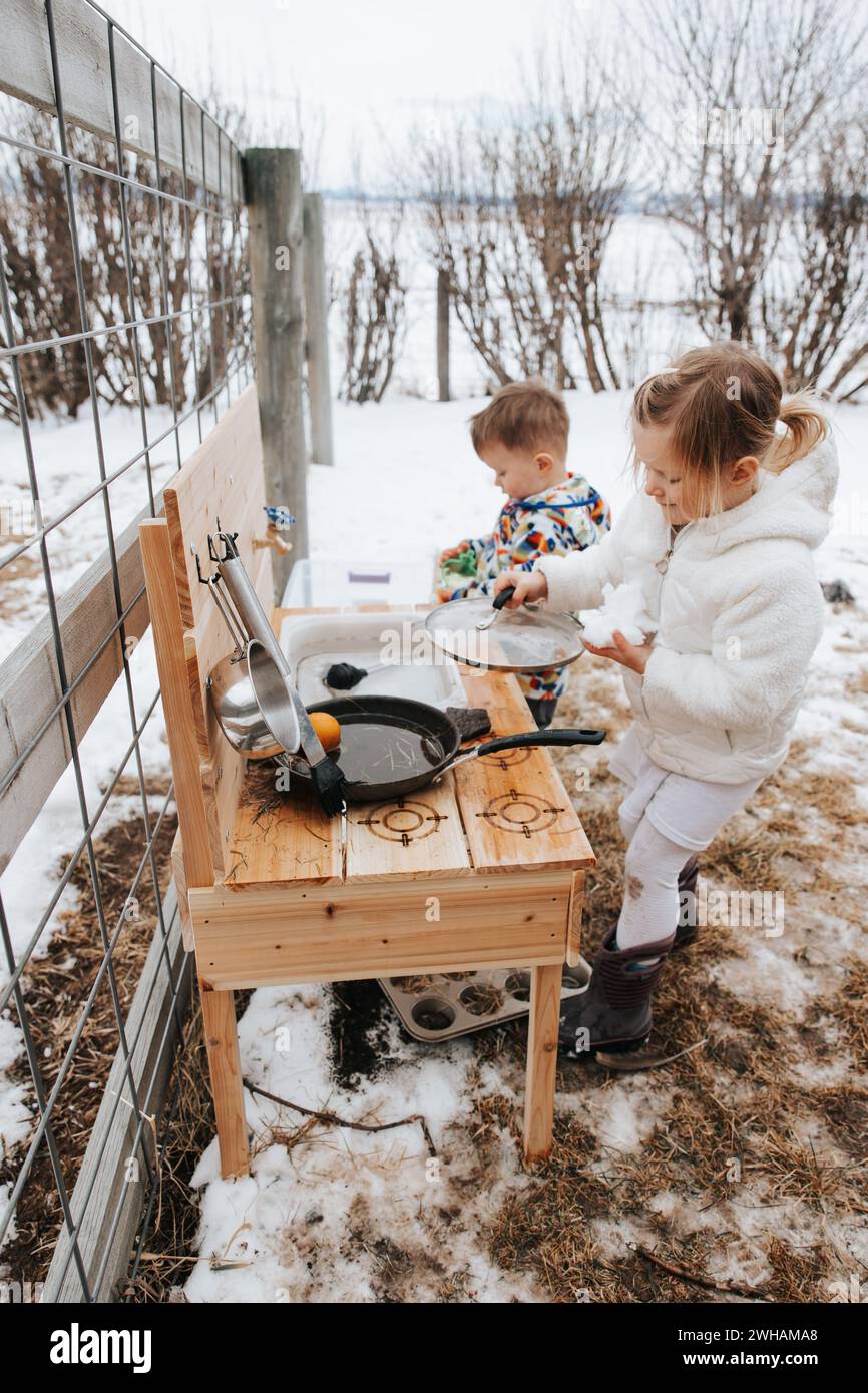 Siblings play in snowy mud kitchen, winter fun Stock Photo - Alamy