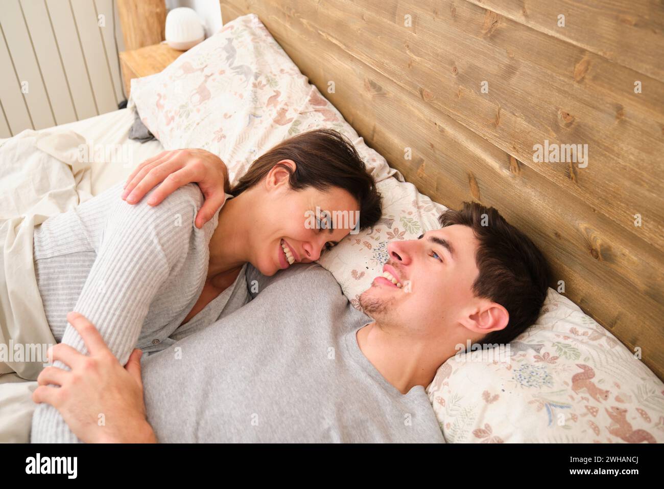 Spanish couple smiling while lying on bed in the morning Stock Photo ...