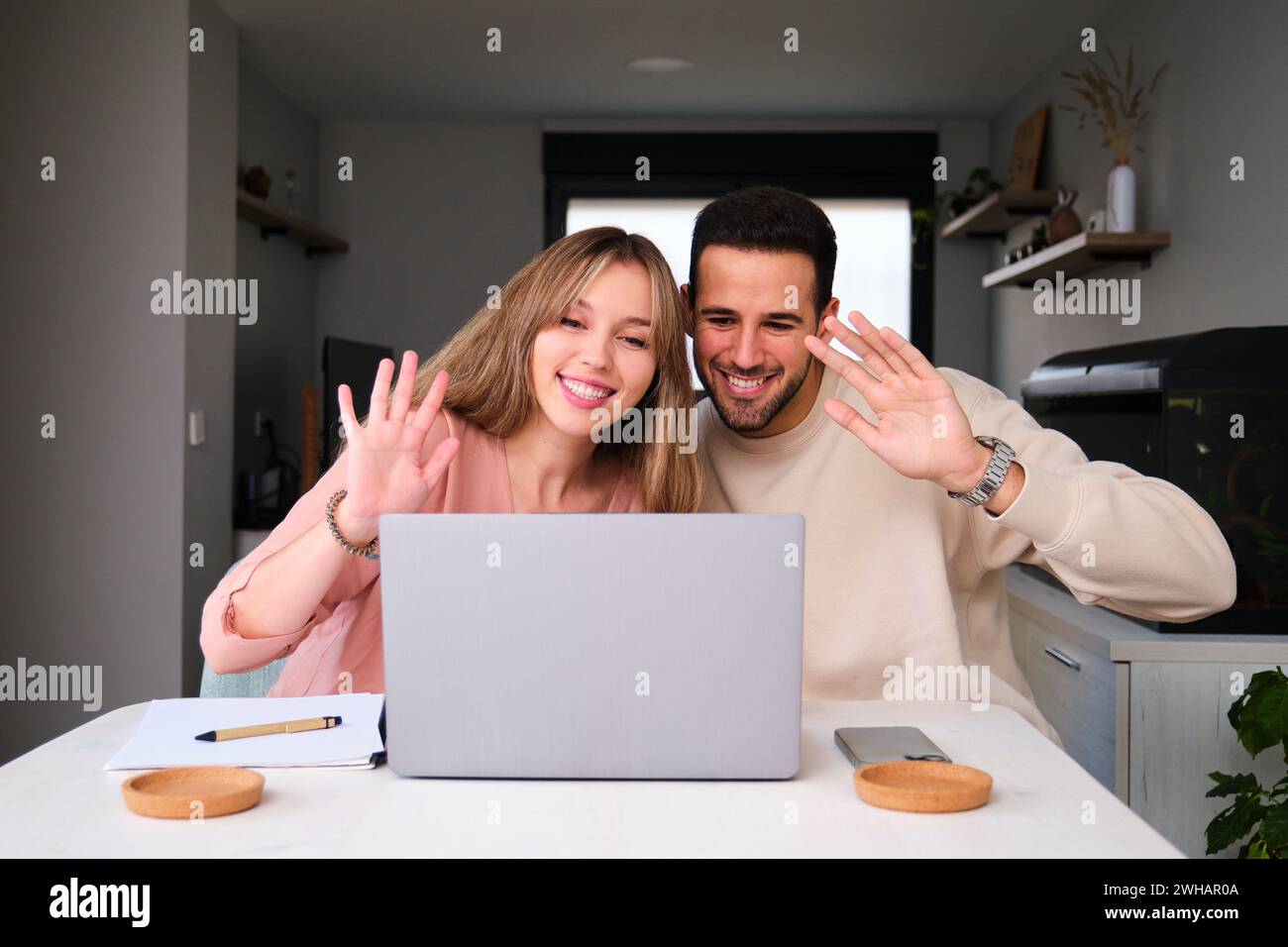 Spanish couple waving on a video call with family or friends at home ...