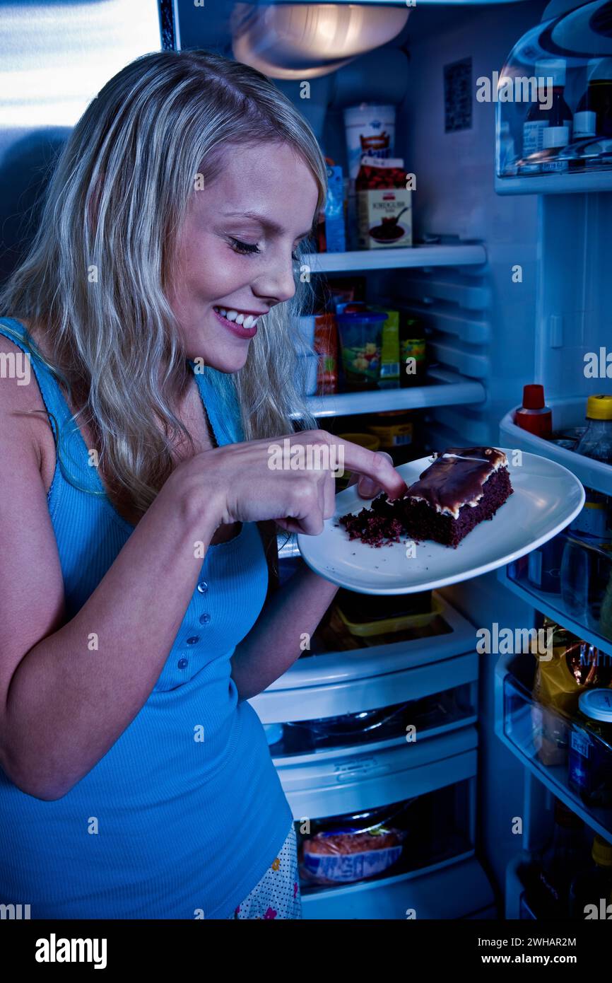 Young woman having a bite of cake at night Stock Photo - Alamy