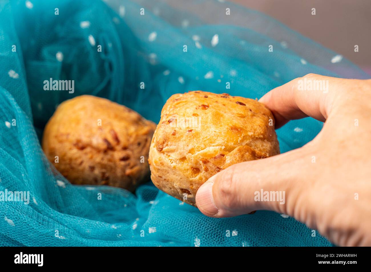 A male hand taking a tasty baked scone on a blue textile background ...