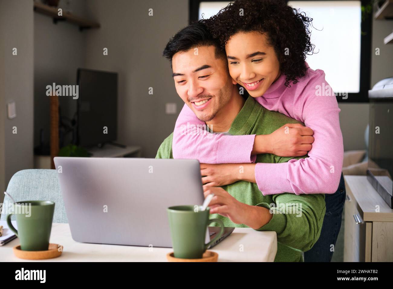 Multiethnic happy couple using the laptop and hugging Stock Photo - Alamy