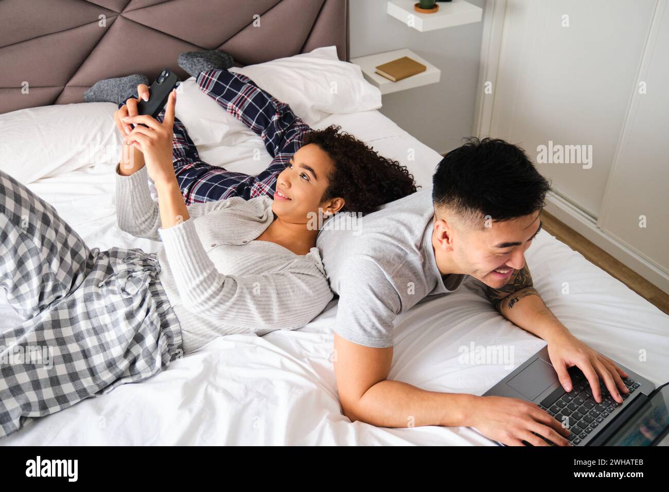 Diverse happy couple using the smartphone and laptop on bed together Stock Photo - Alamy