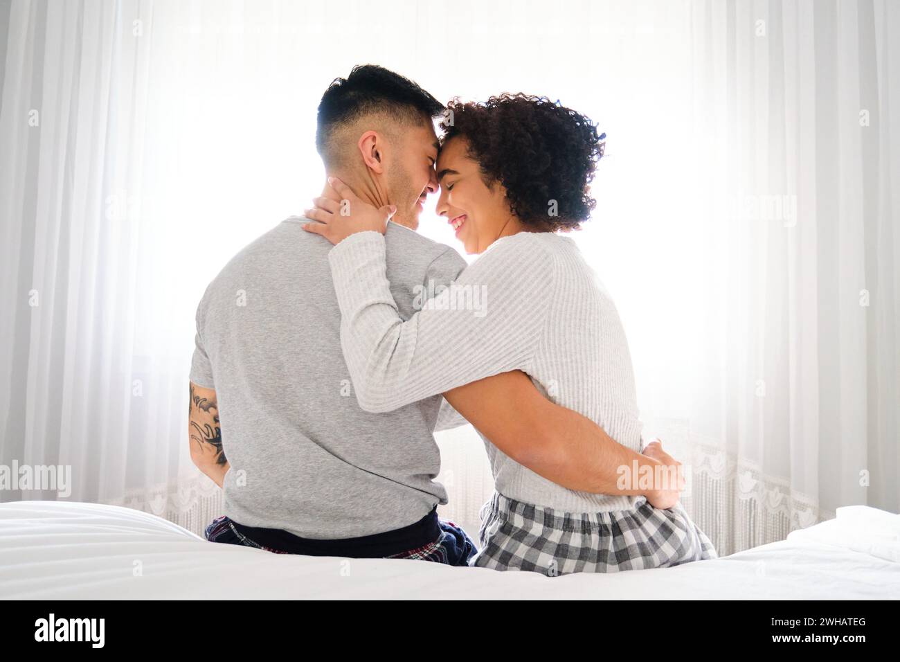 Multiracial romantic couple sitting together in bed backlighting Stock ...