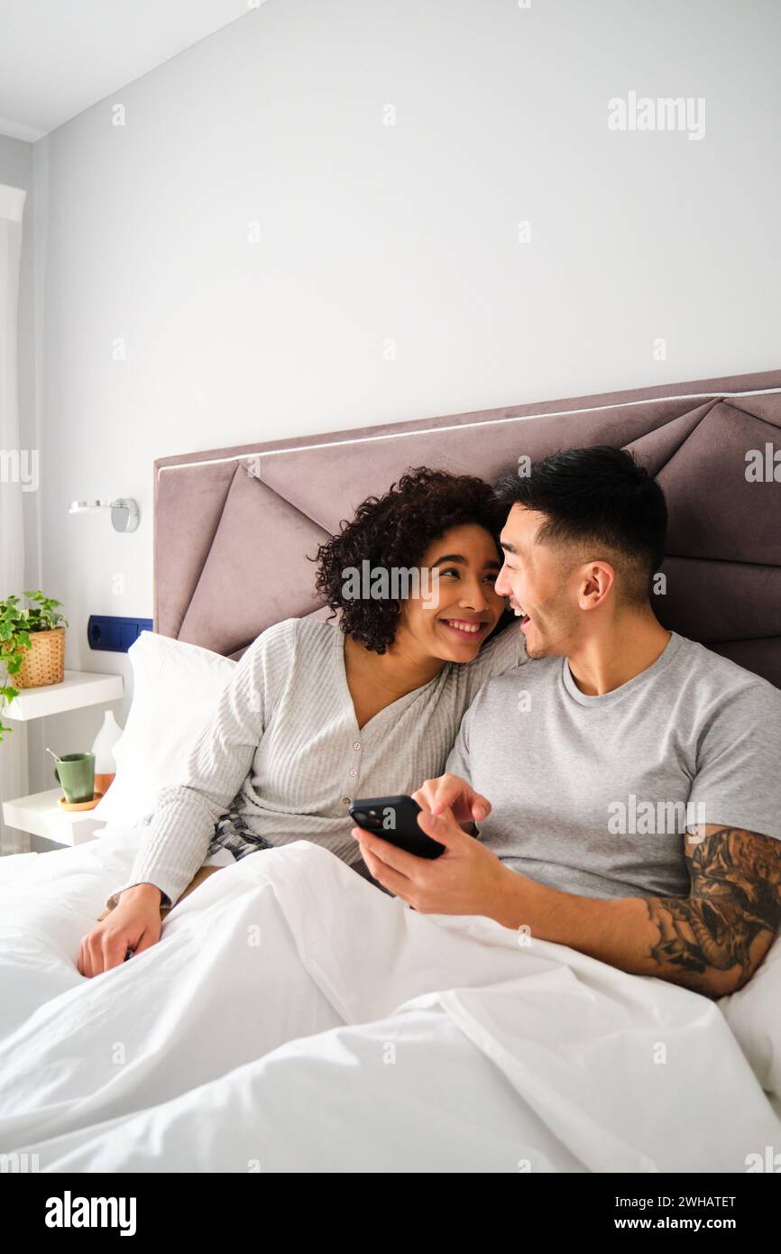 Multiethnic super happy couple using the smartphone on bed Stock Photo - Alamy