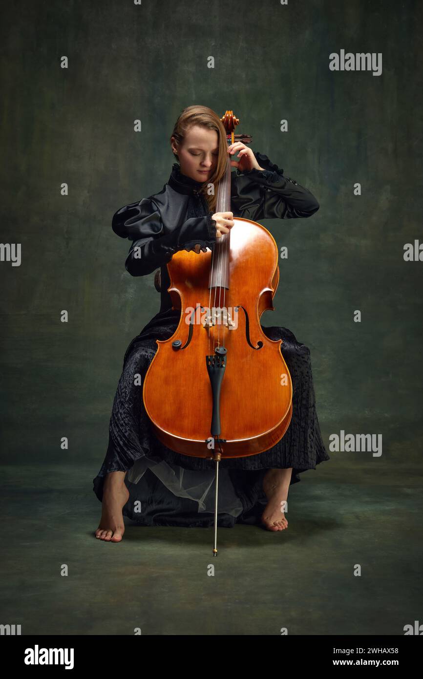 Young woman in black dress, cellist sitting on chair and playing cello ...