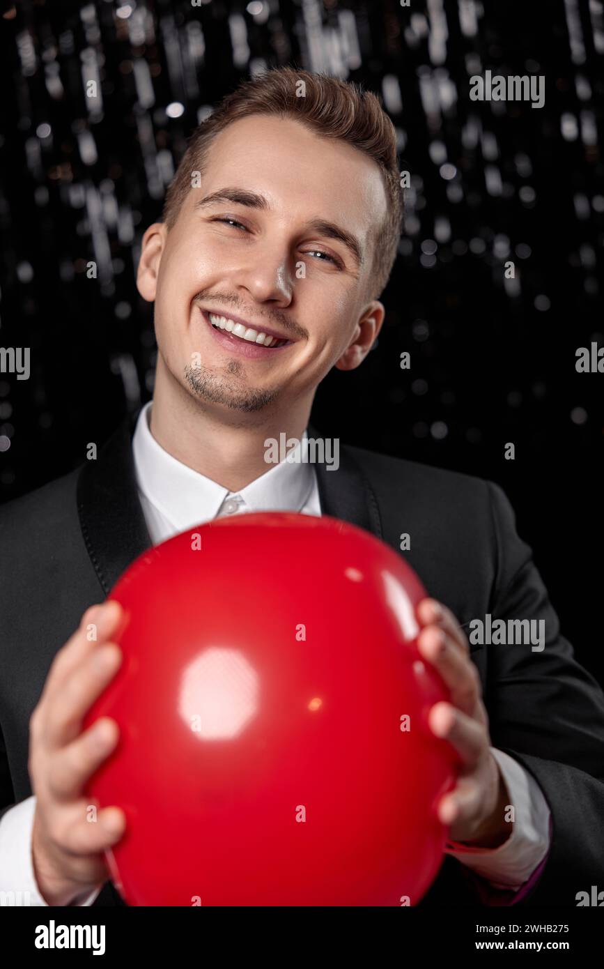 caucasian man in black jacket with red air balloon on dark glitter ...
