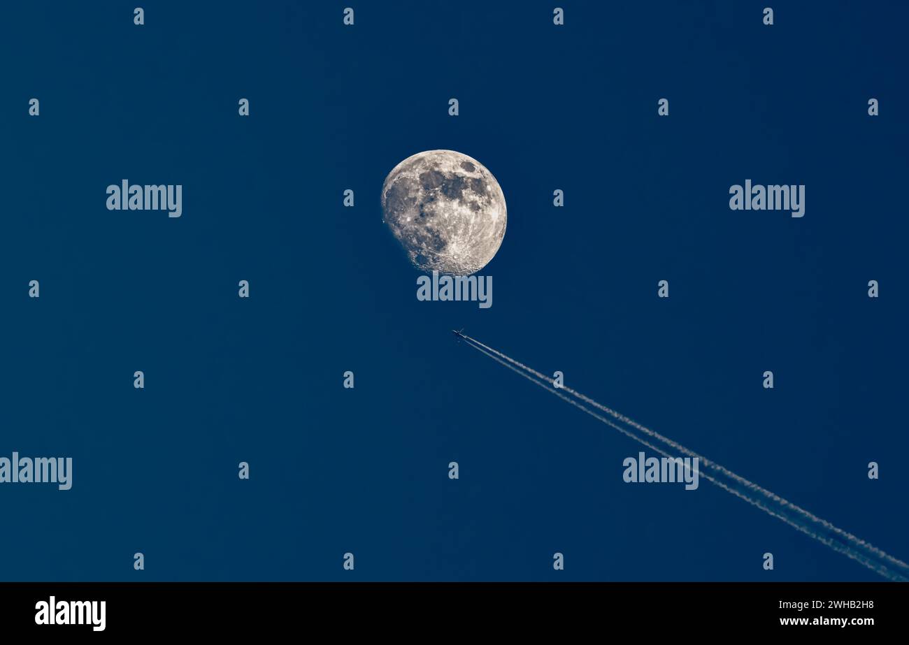 A plane passing the moon in the sky leaving a trail of smoke Stock ...