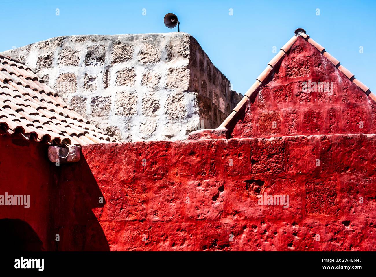 house with red wall and brown tiled roof with stone wall and blue sky ...