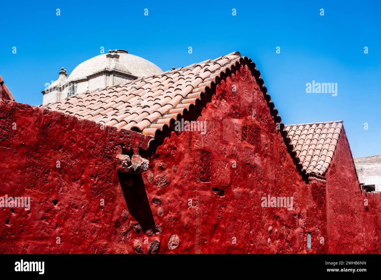 house with red wall and brown tiled roof with stone wall and blue sky ...
