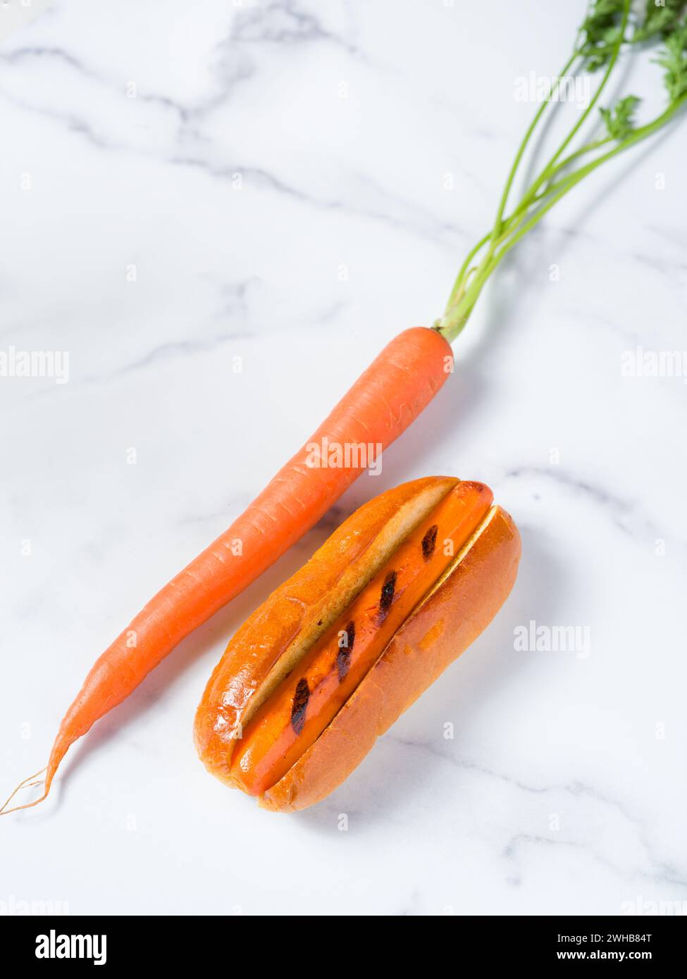 Meat alternative of a carrot dog and a raw carrot on a marble surface ...