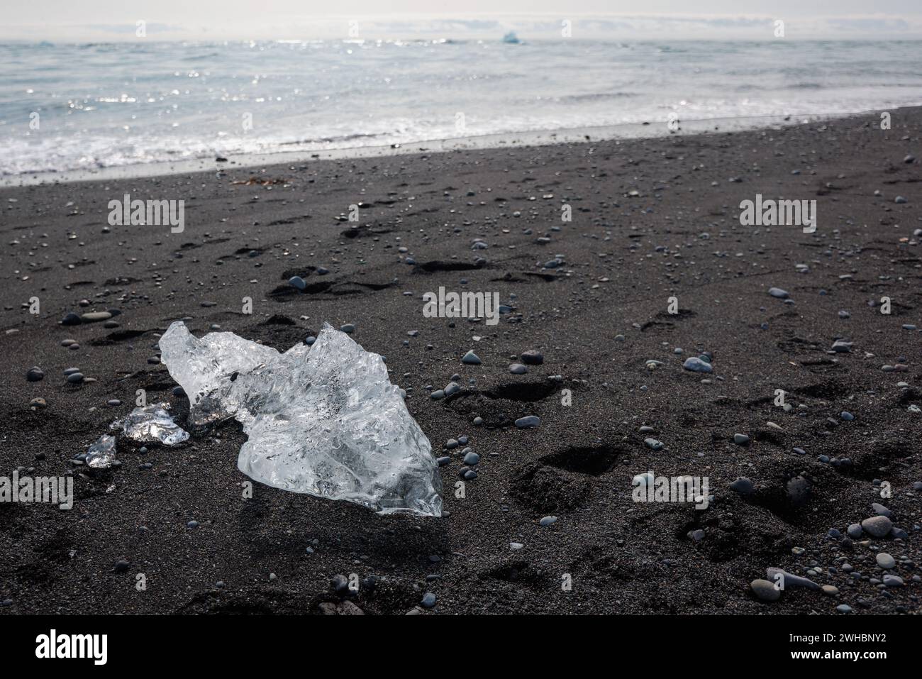 Ocean waves lapping up chunks of ice sparkling in the sun on a black ...