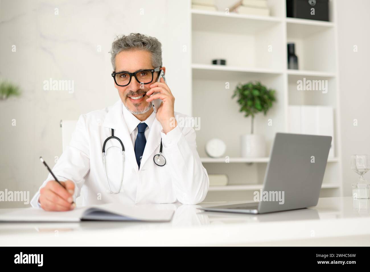 A seasoned doctor with grey hair is jotting down notes while ...
