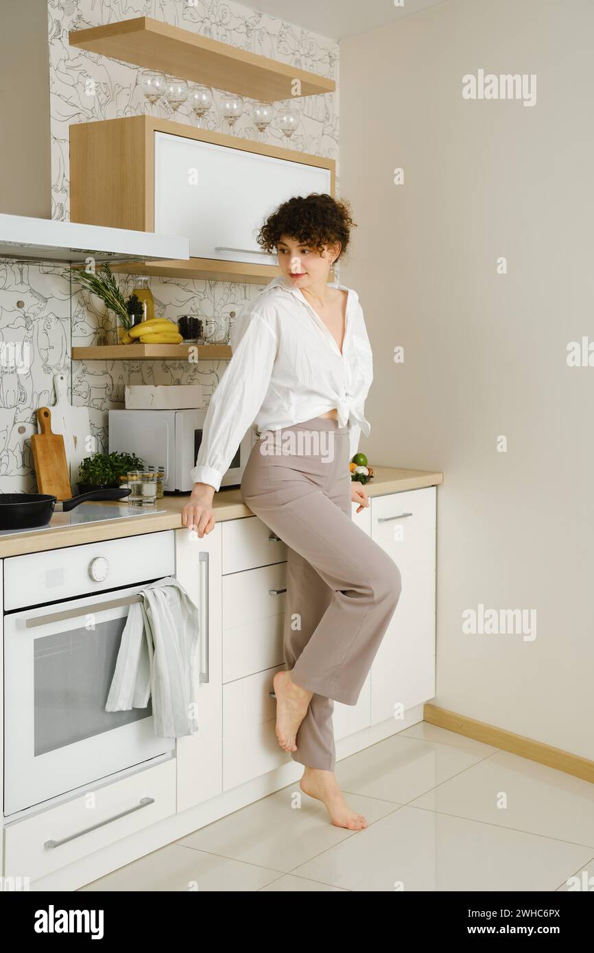 Young barefoot woman standing by the countertop of a well-lit and ...