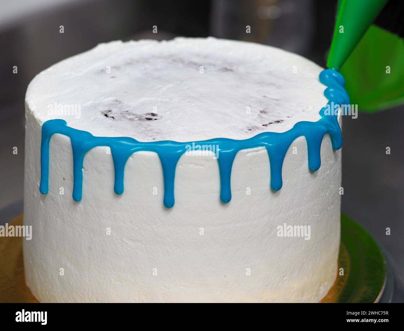 A white frosted cake in the process of being decorated with blue icing ...