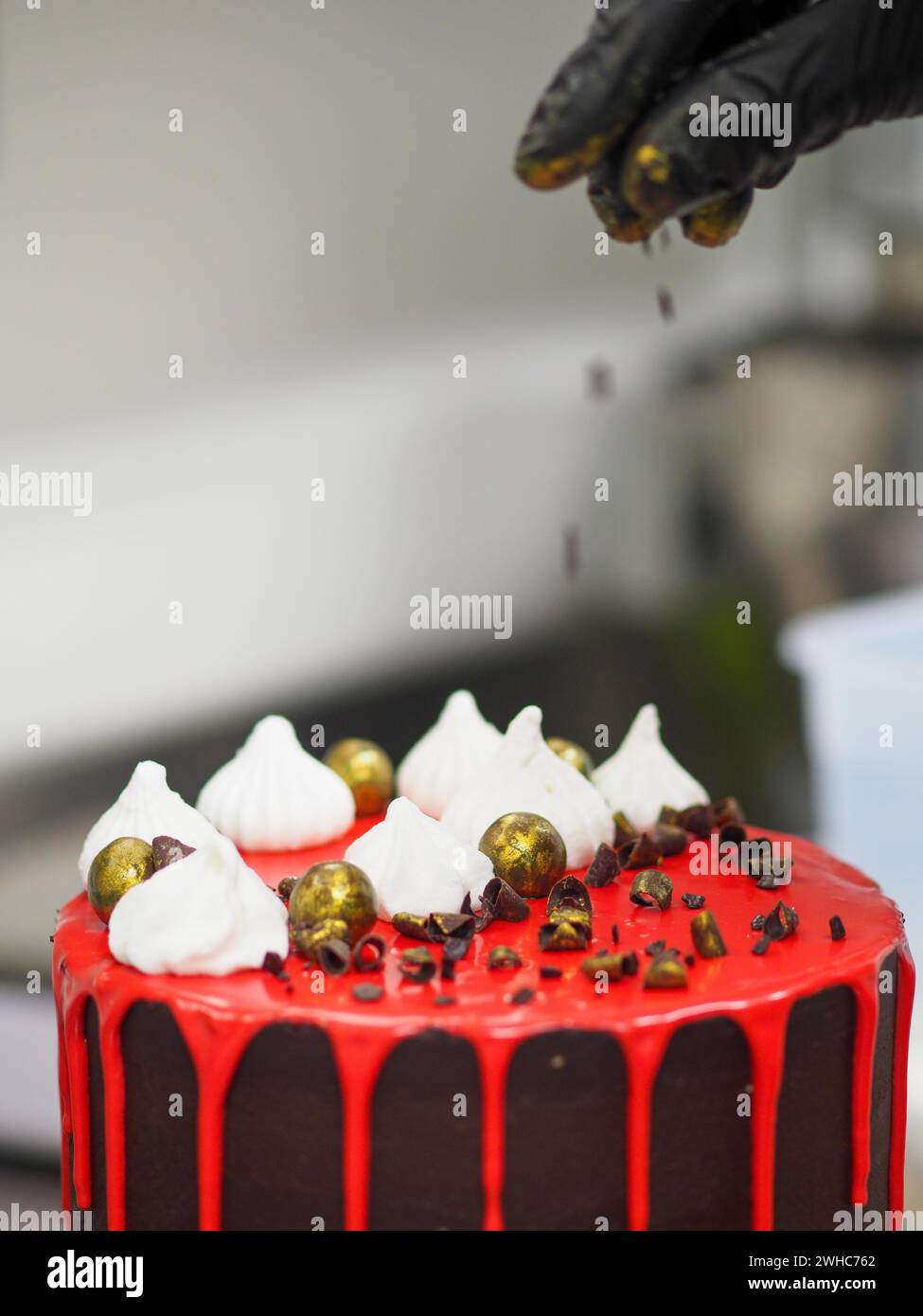 Chef sprinkling gold dust chocolate over a frosted dripping red brown ...