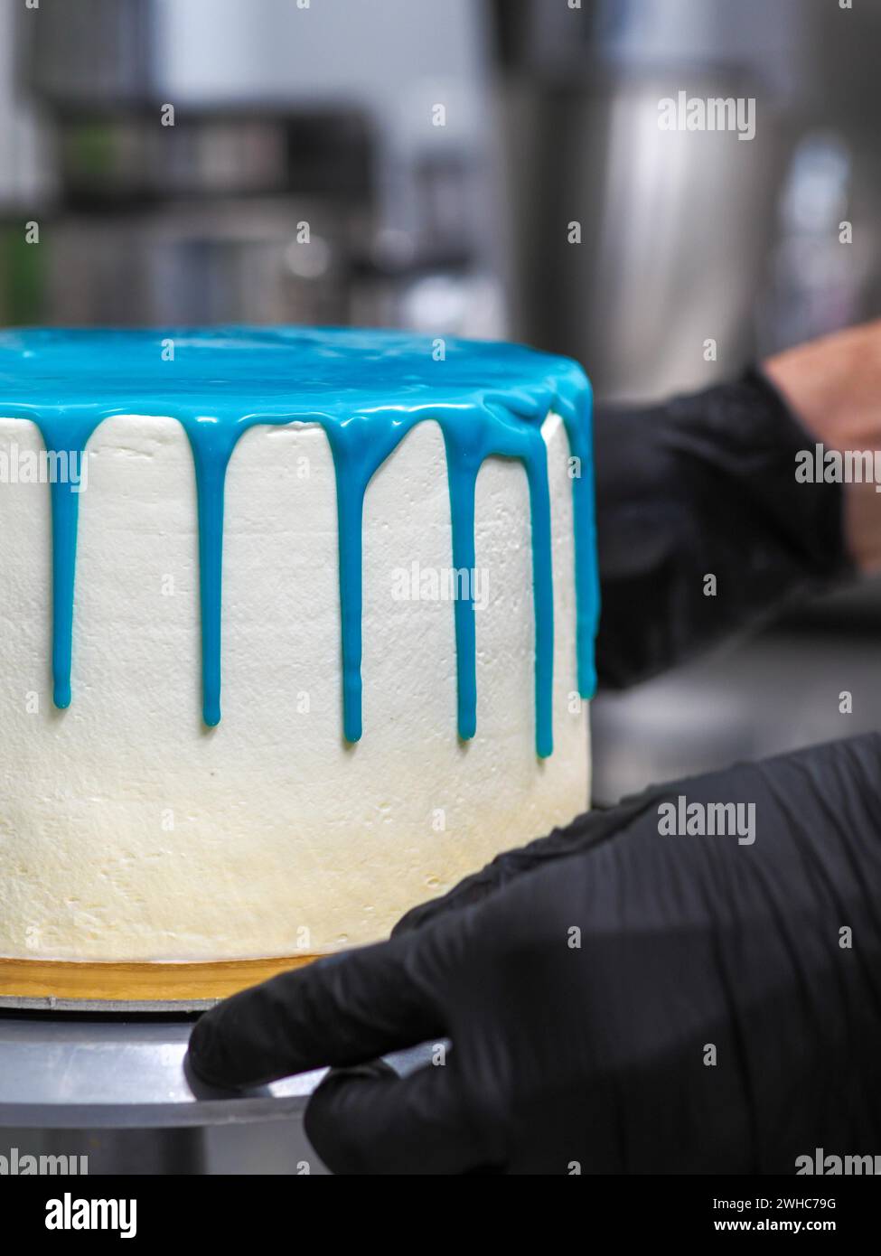 A pastry chef applying blue icing on a white cake, highlighting the ...