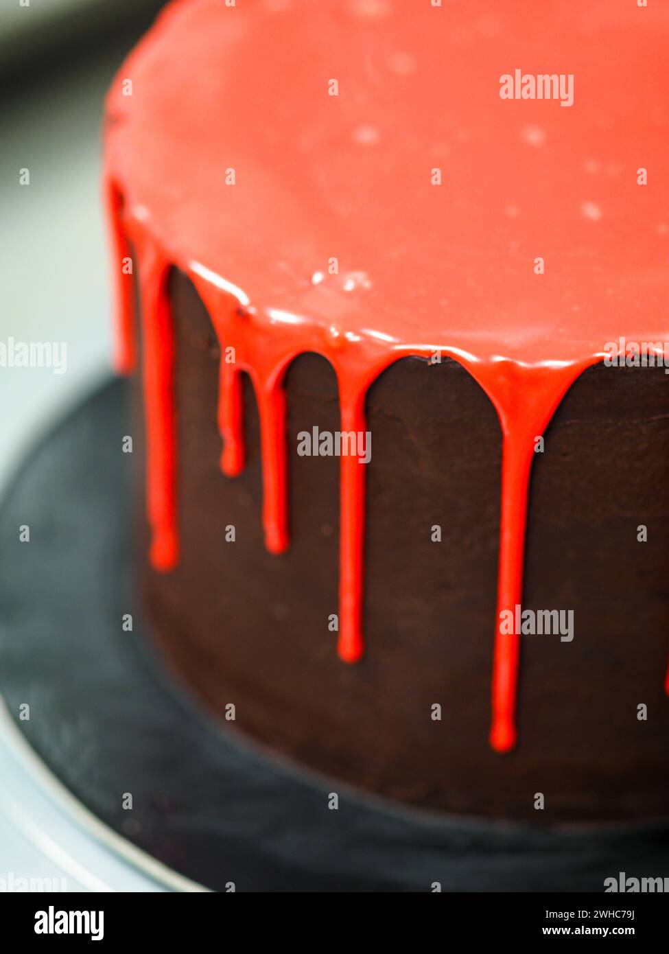 A chocolate cake with red dripping icing on a black surface, creating a ...