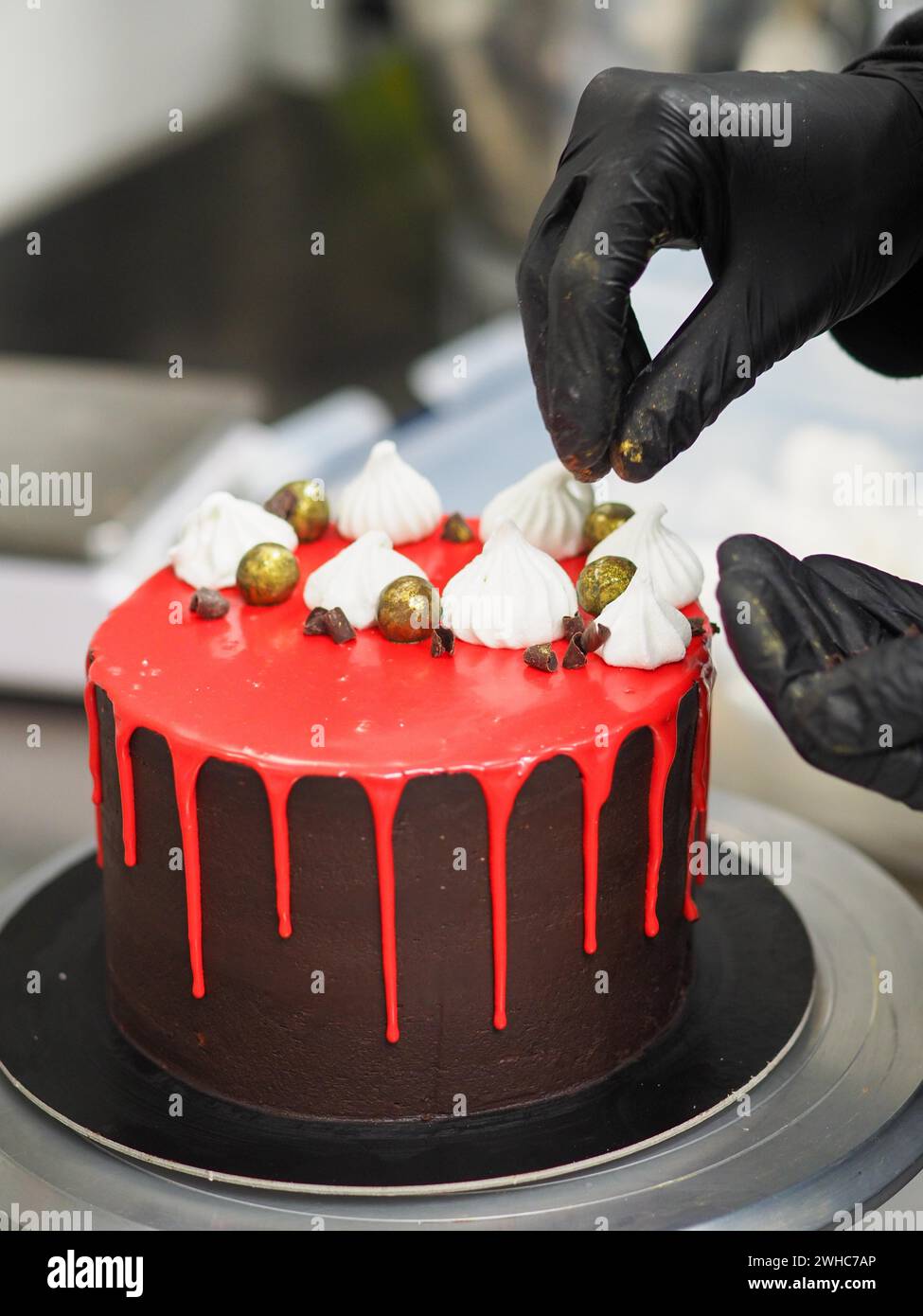 Finishing touches being applied to a chocolate cake with red dripping ...
